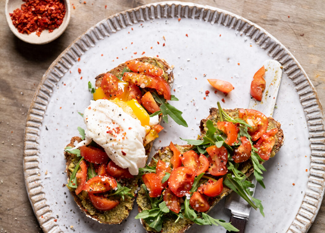 Brotscheibe mit Spinat-Pesto, frischem Rucola, Tomaten und pochiertem Ei
